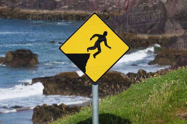 A yellow warning sign depicting a person falling off a cliff;County ...