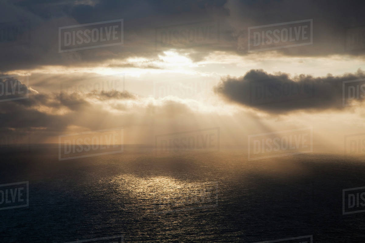 Sunlight streaming through the dark clouds and reflecting on the ocean ...