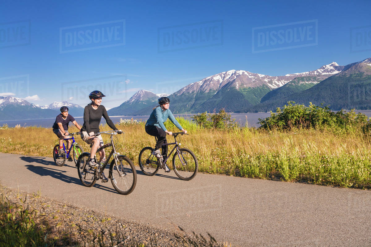 Two women and a man biking on the bird point to girdwood bike trail ...