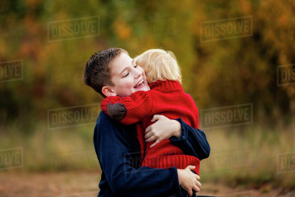 Boy shares an embrace with his young brother outdoors in a park in ...