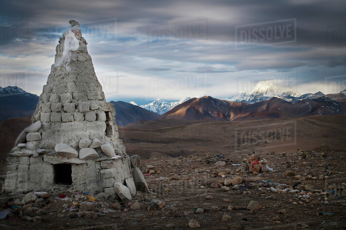 A stone conical structure on a barren landscape with mountains in the ...