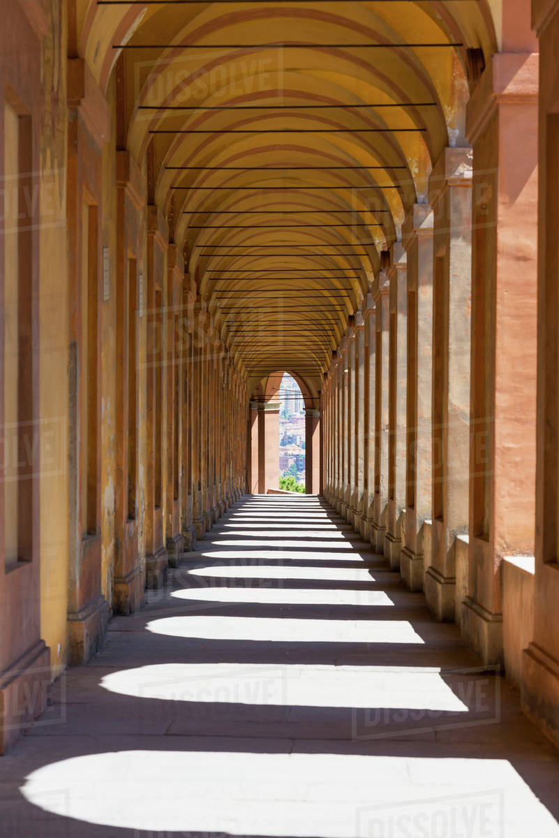 An outside corridor with arched roof and shadows of arches cast on the ...