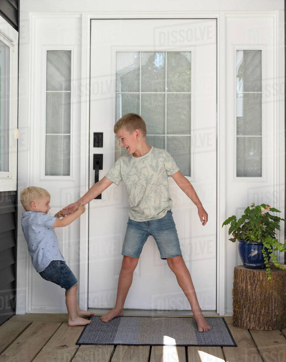 Two young brothers playing at their home, standing outside their front ...