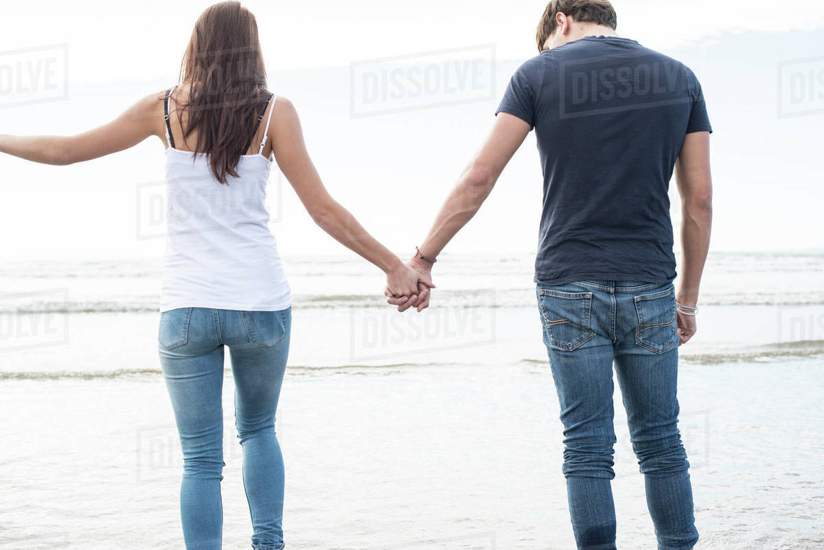 A young couple walk holding hands across the beach at Porthmadog ...