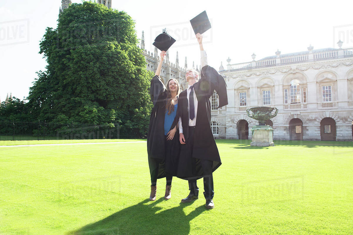 Two young students in graduation gowns throwing mortar boards into the ...