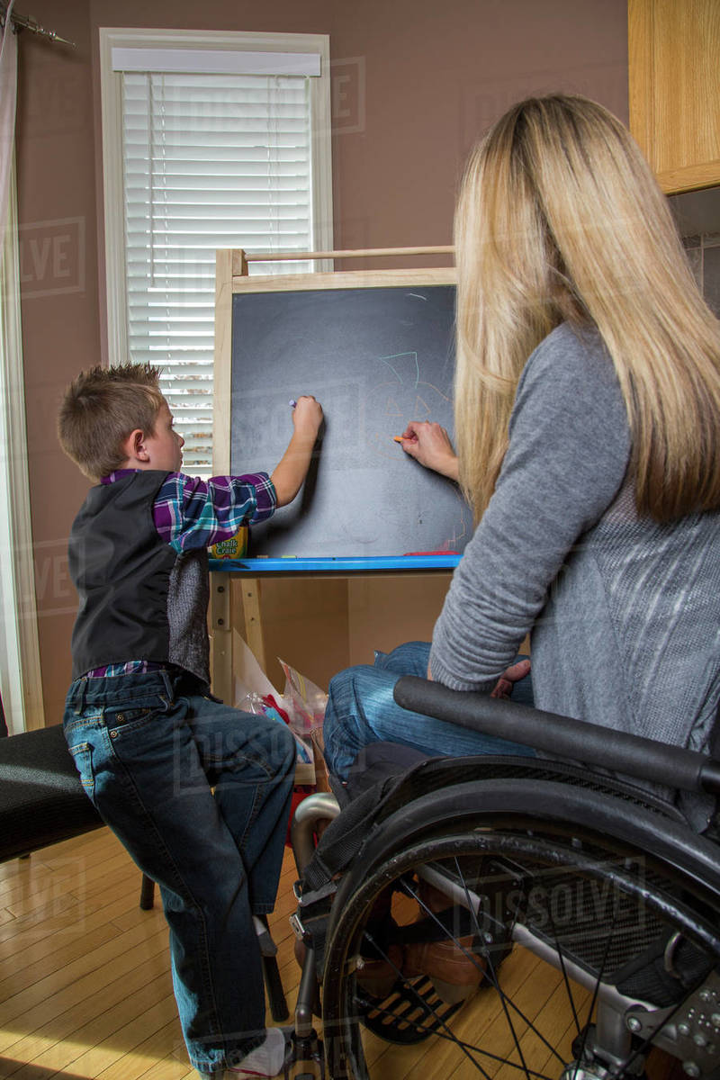 Young paraplegic mother teaching her son and drawing on a chalkboard ...