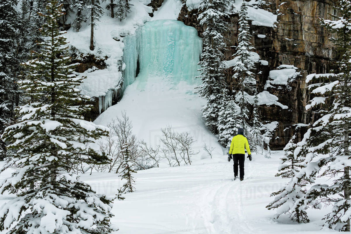 Female snowshoeing along a snow-covered trail with an ice falls on a ...
