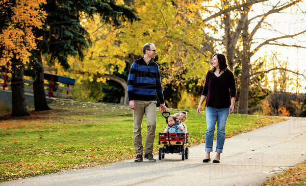 A father and mother pulling their young children in a wagon in a city ...