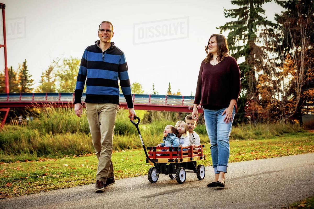 A father and mother pulling their young children in a wagon in a city ...