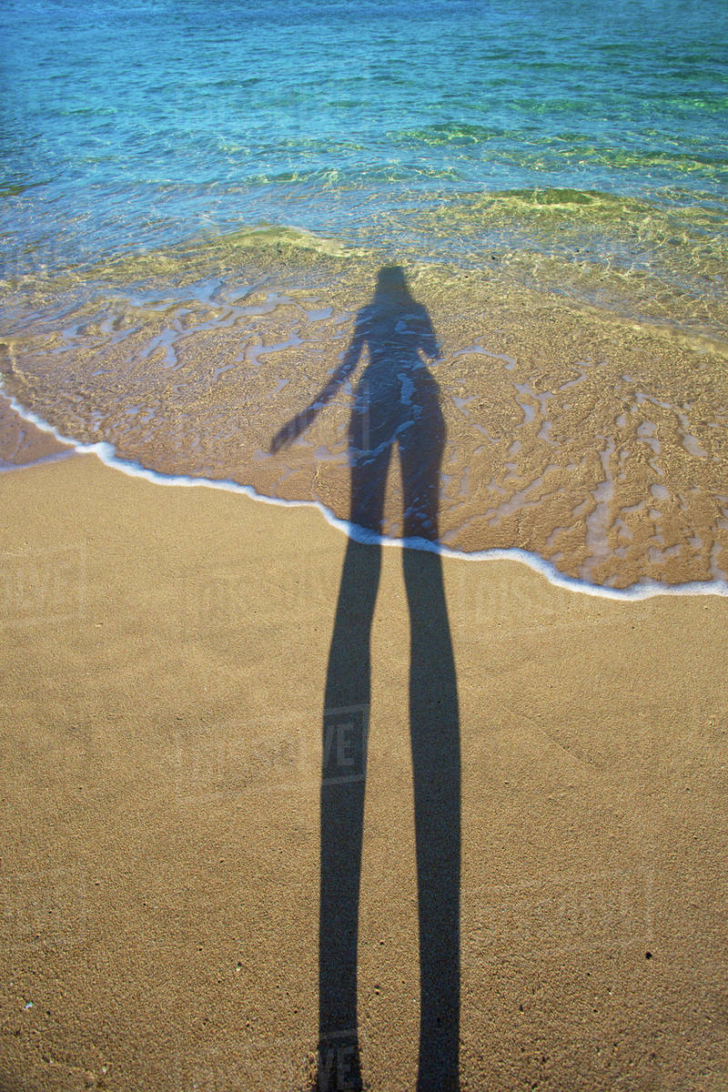 Shadow of a woman standing on the beach at the water's edge; Kauai ...