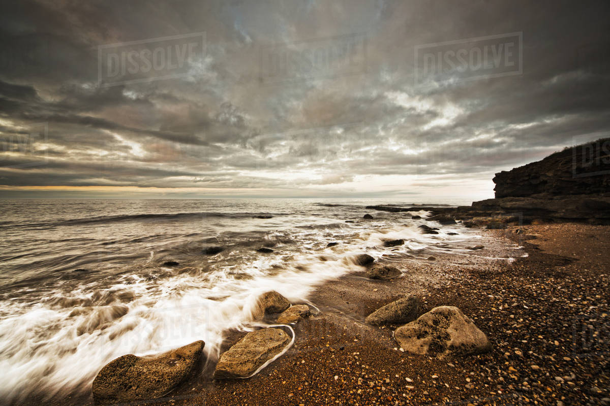 Water washing up on the shore along the coastline under a cloudy sky ...