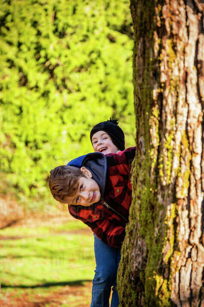 Two young boys peeking out from behind a tree with big smiles on their ...