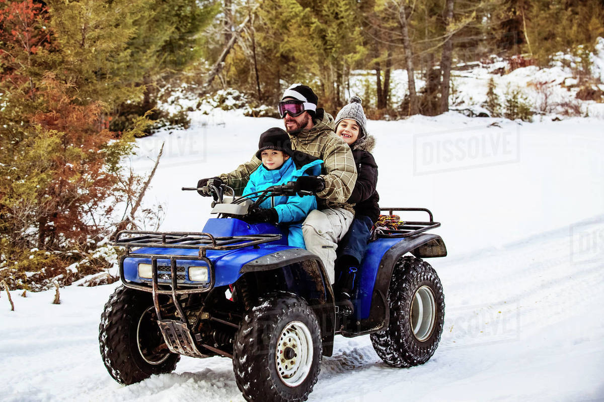 A Man And Two Young Boys Riding An ATV On A Snowy Trail In A Mountain ...