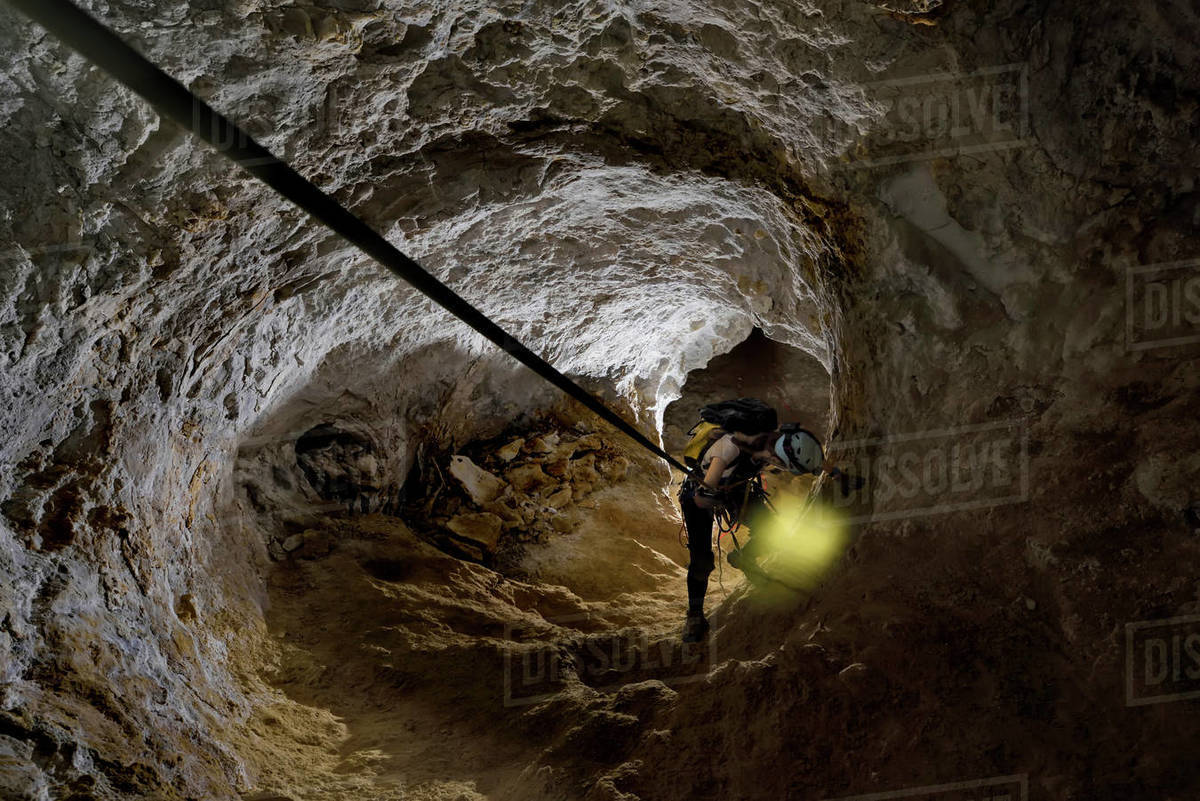 A cave explorer searches for a foothold while climbing up a rope ...