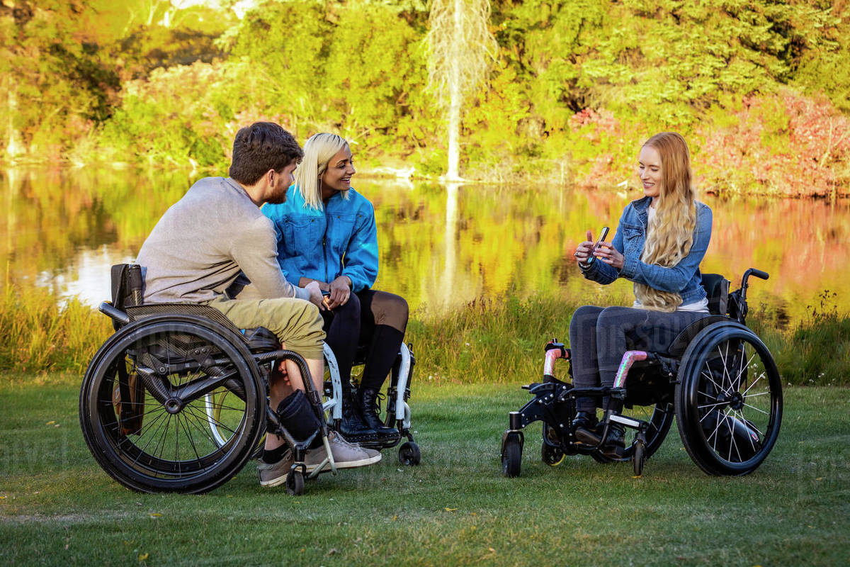 Group of three young paraplegics in their wheelchairs visiting together ...
