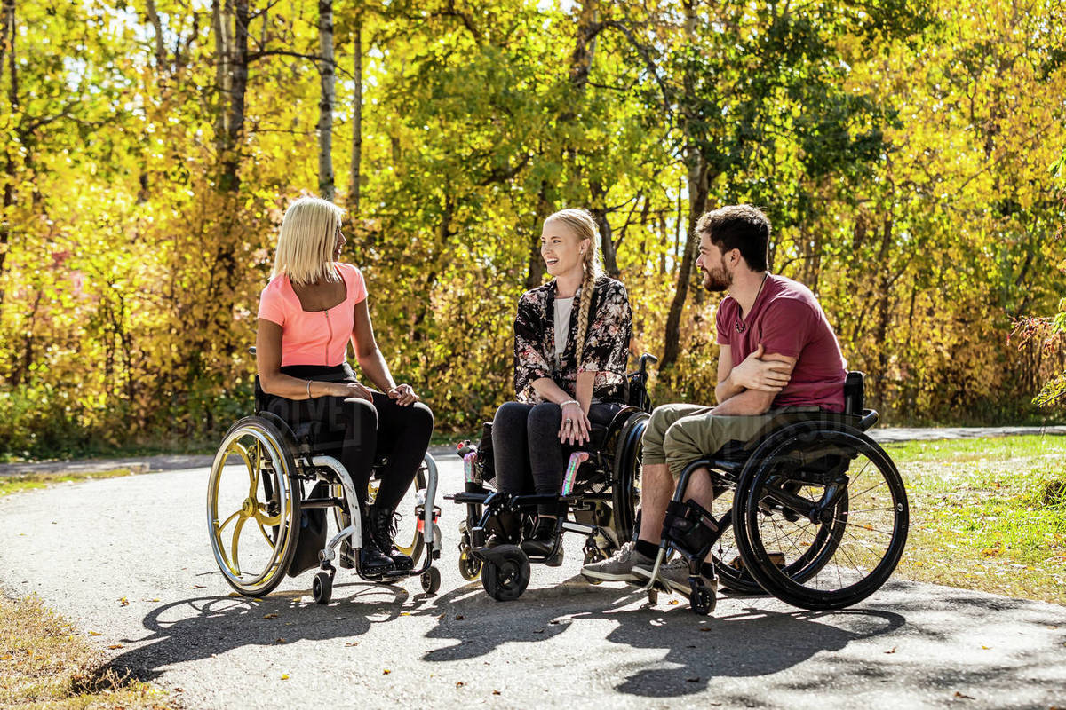 Group of three young paraplegics in their wheelchairs visiting together ...