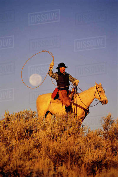 Cowboy sitting on horse with a full moon captured in his lasso; Seneca ...