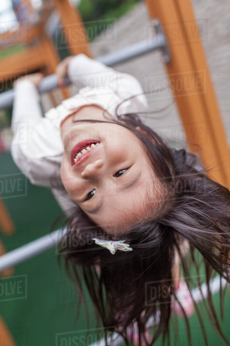 Young girl hanging upside down on climbing equipment at a playground; Hong Kong, China - Royalty ...