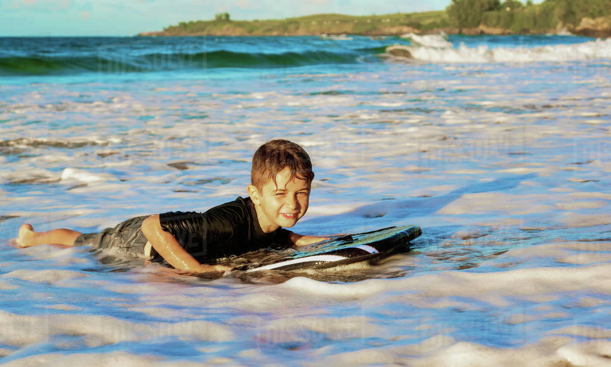 A young boy riding a wave on a bodyboard into the shore at D. T ...
