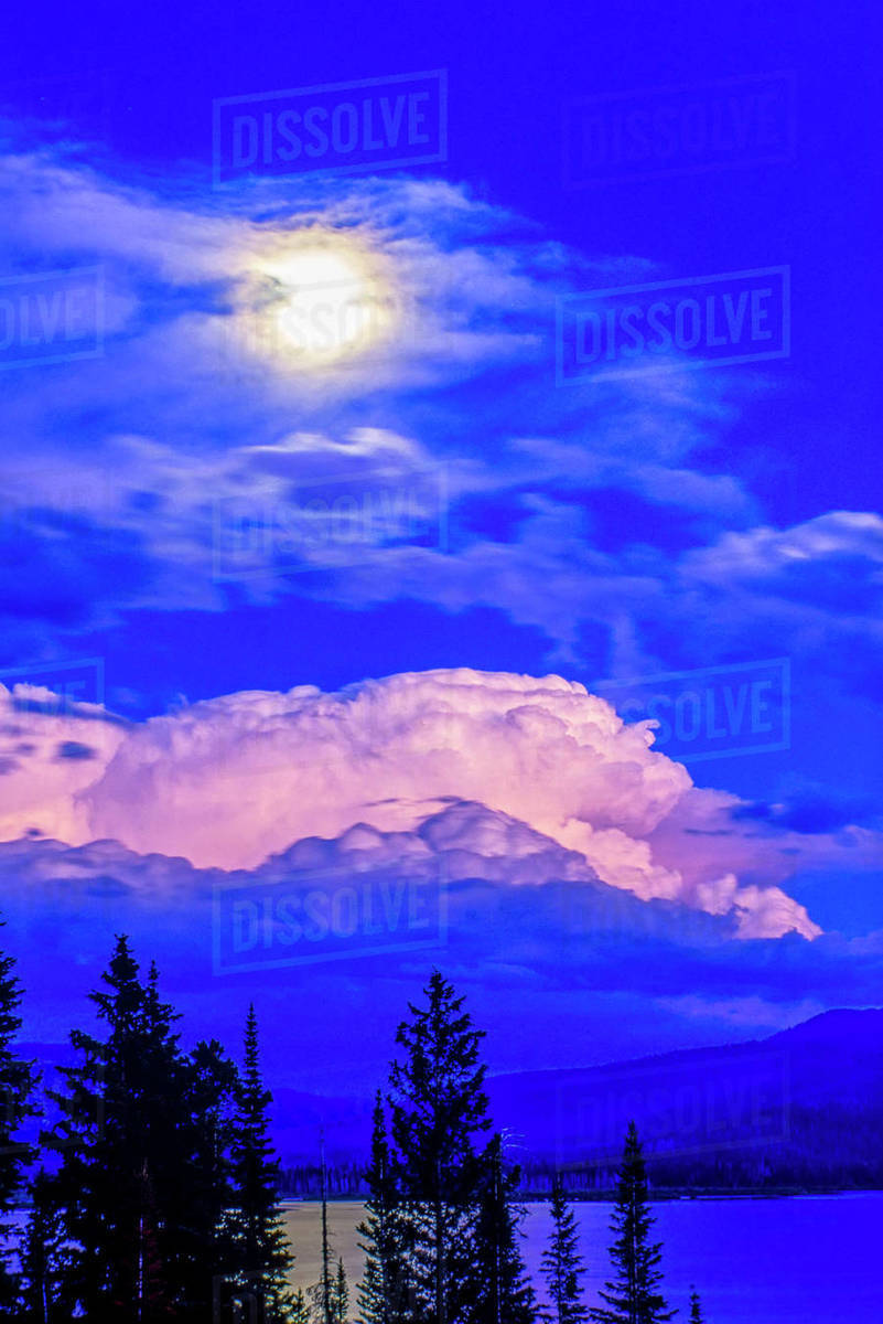 Full Moon in a blue sky lighting up the pink thunder clouds over the ...