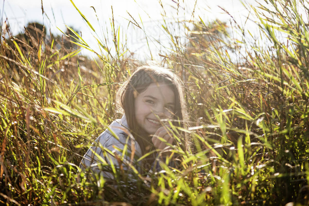 Preteen girl sits in the tall grasses of a farm field, smiling and ...
