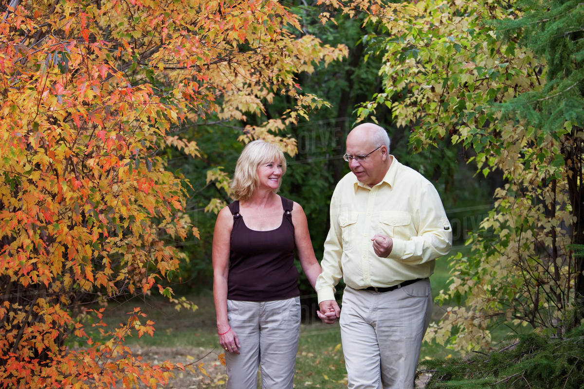 Mature married couple walking together in park during fall season ...