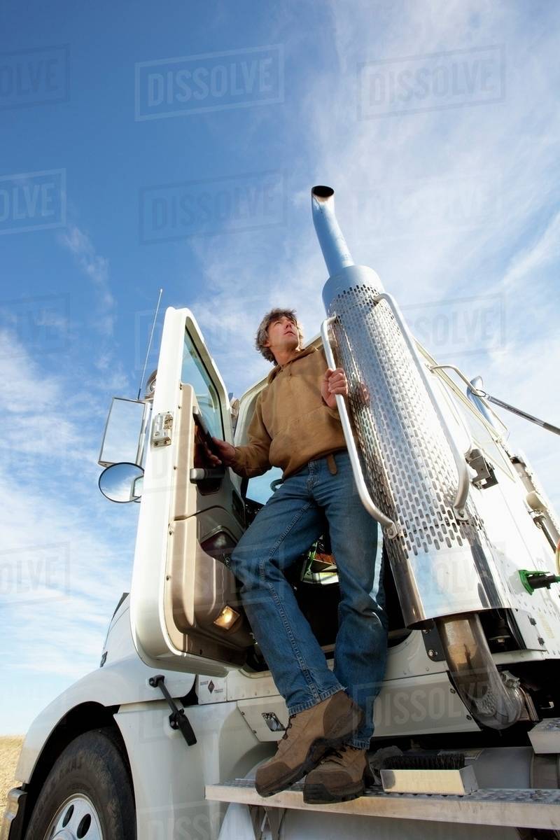 A Man Standing On The Step Of The Cab Of His Truck; Three Hills ...