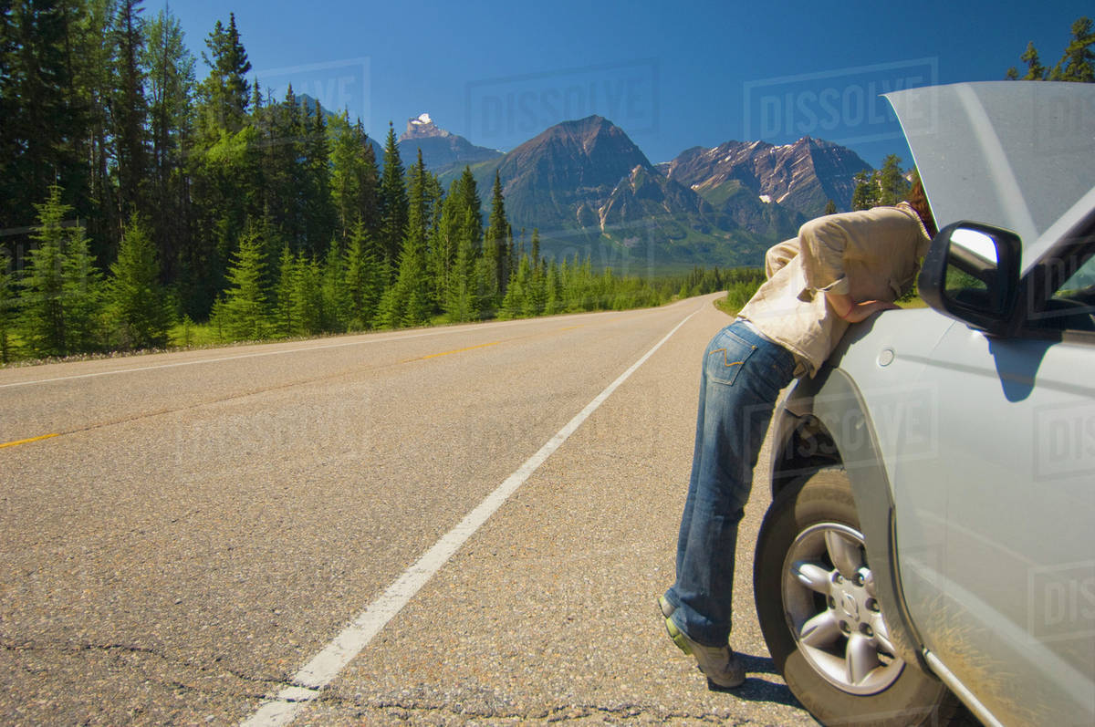 Woman Looking Under Hood Of Her Car On Mountain Road; Alberta Canada ...
