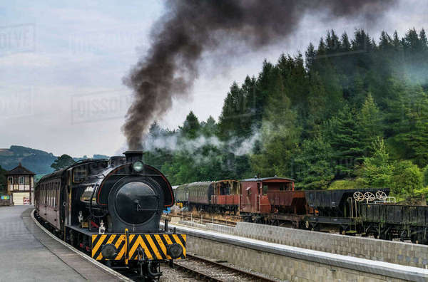 A train sits at a station with black smoke billowing from the engine ...