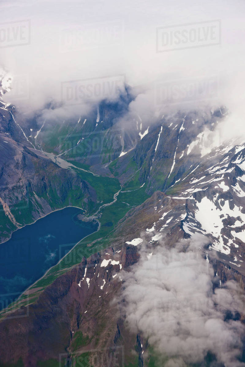 Aerial view of clouds obscuring peaks with a lush green valley and lake ...