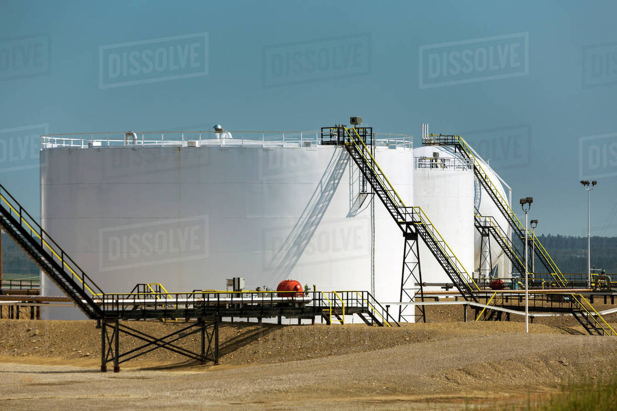 Large white metal oil storage tanks with black stairs and blue sky ...