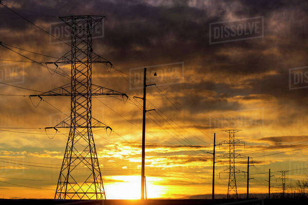 Silhouette of large metal powerline towers with colourful clouds and ...