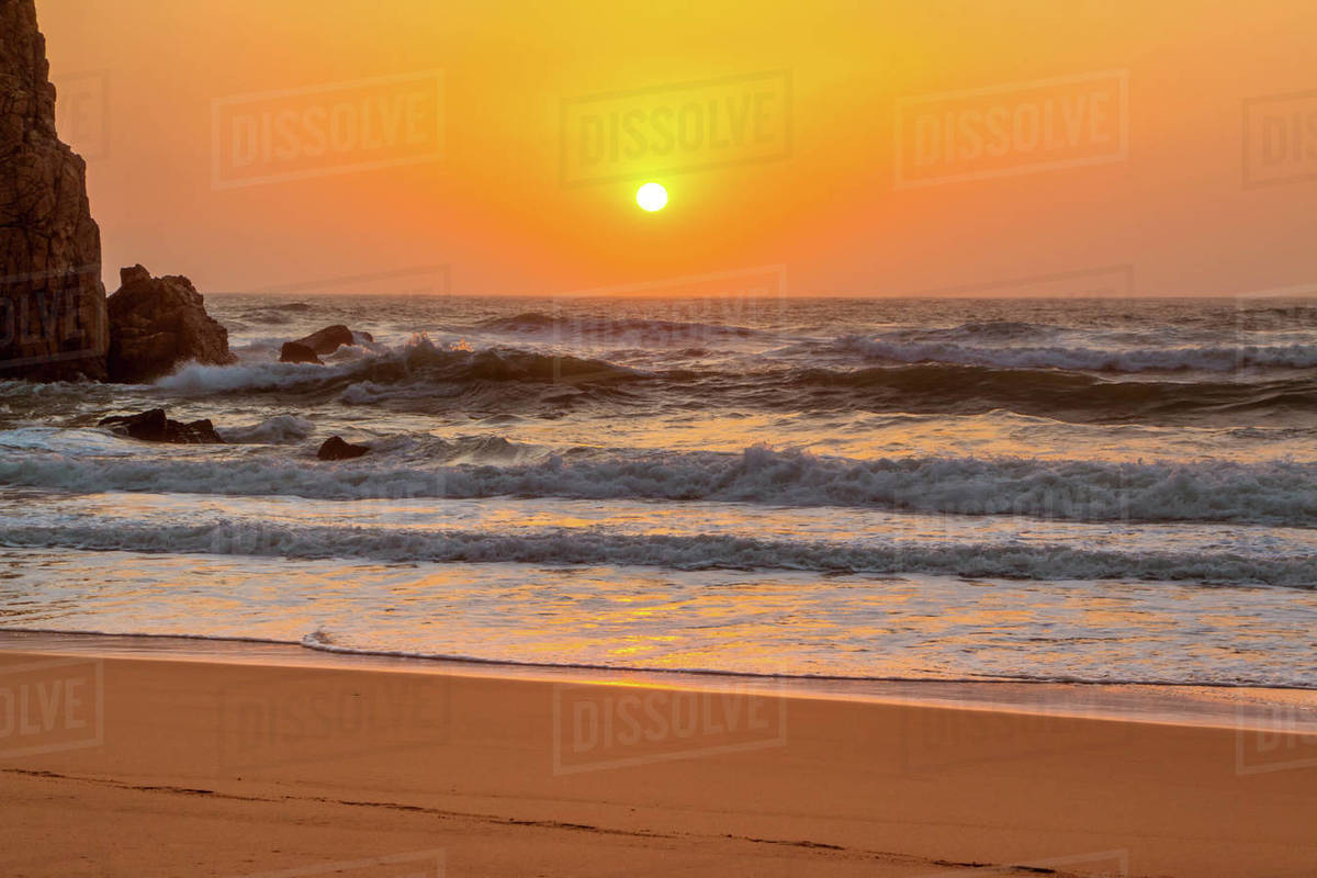Portugal. Sandy beach near Cape Roca. Rock and surf waves. The sun sets ...