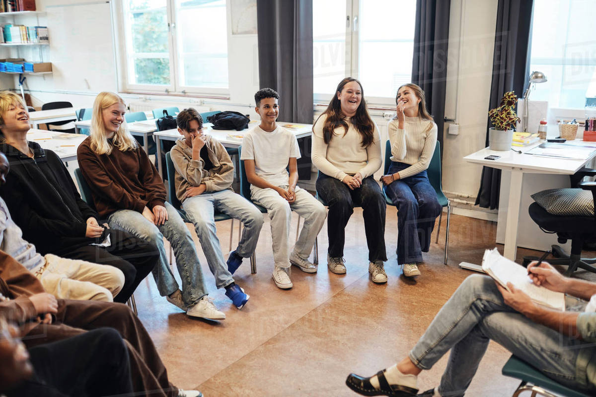 Happy male and female students sitting with counselor in group therapy ...
