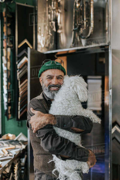 Portrait of smiling craftsman hugging pet dog in frame shop - Royalty ...