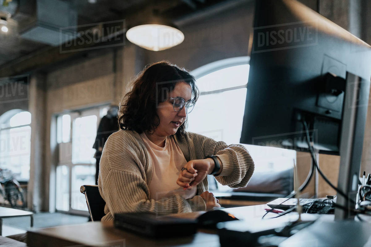 Female computer programmer checking time on wristwatch while working at ...