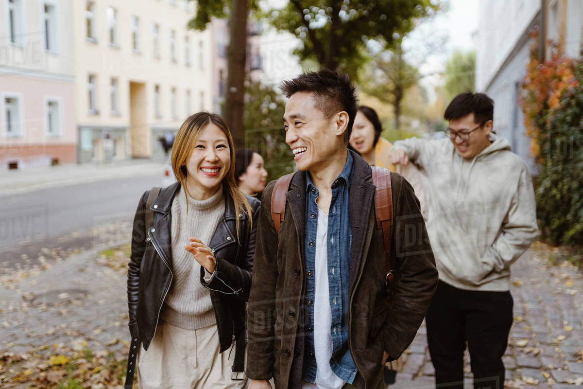 Male and female friends laughing while walking on sidewalk - Royalty ...