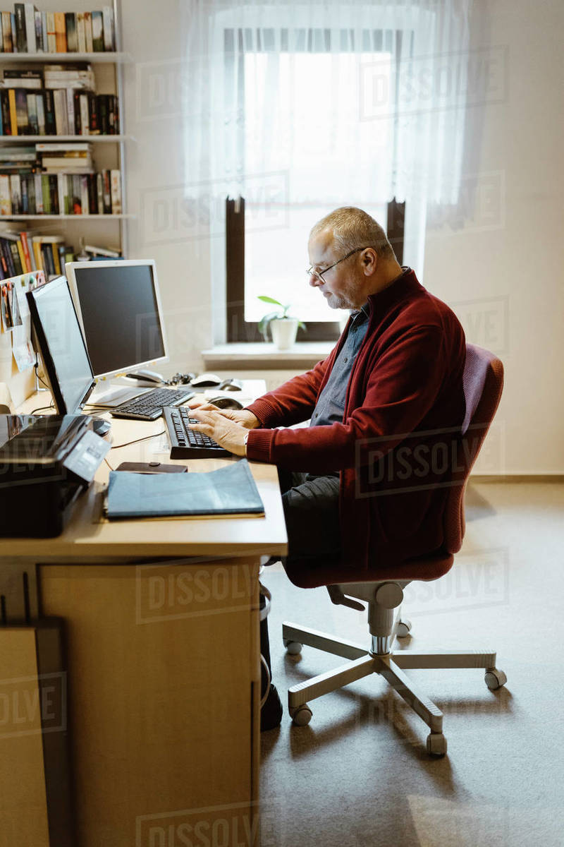 Full length of senior man typing while using computer at desk in home ... Full length of senior man typing while using computer at desk in home ...