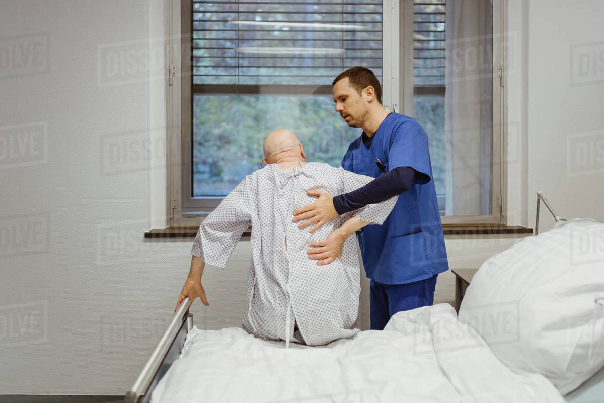 Male nurse helping senior patient sitting on bed at hospital - Royalty ...