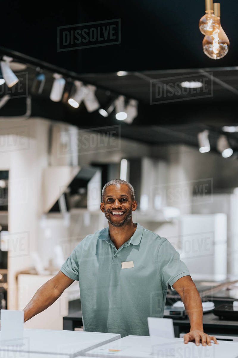 Portrait of happy mature salesman standing at counter in electronics ...