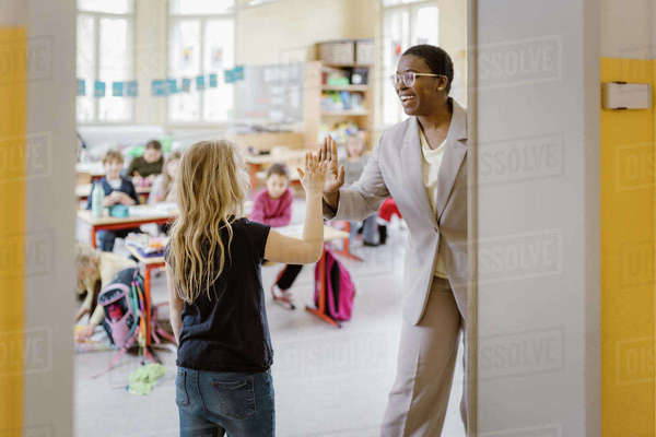 Smiling female teacher and schoolgirl giving high-five at doorway in ...