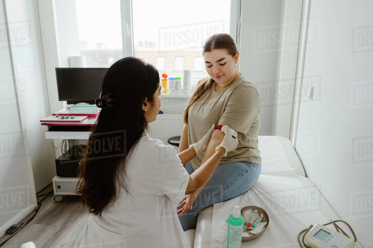 Doctor tying band on patient's arm sitting on bed in clinic - Royalty ...