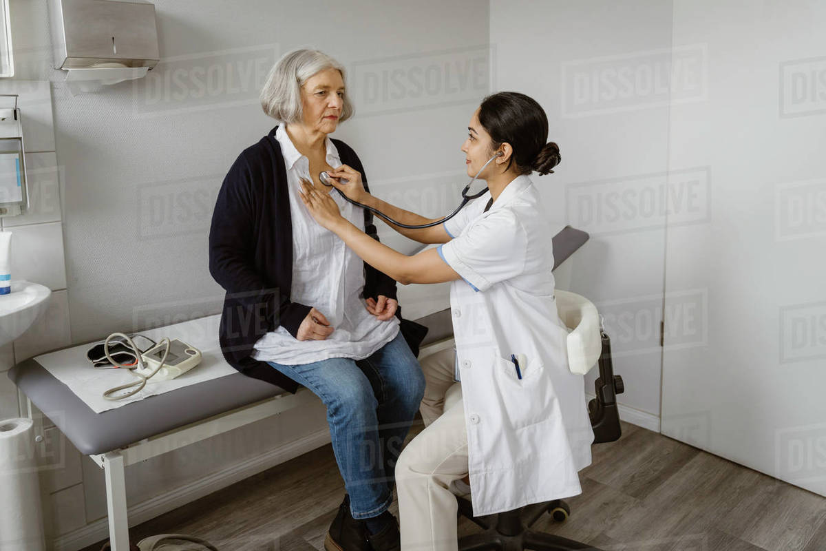 Side view of female doctor listening heartbeat of senior patient ...