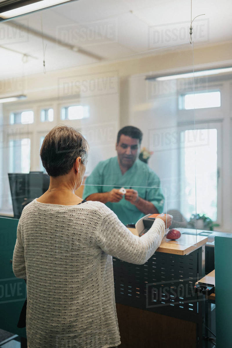 Senior female patient signing in at reception desk in hospital - Stock ...
