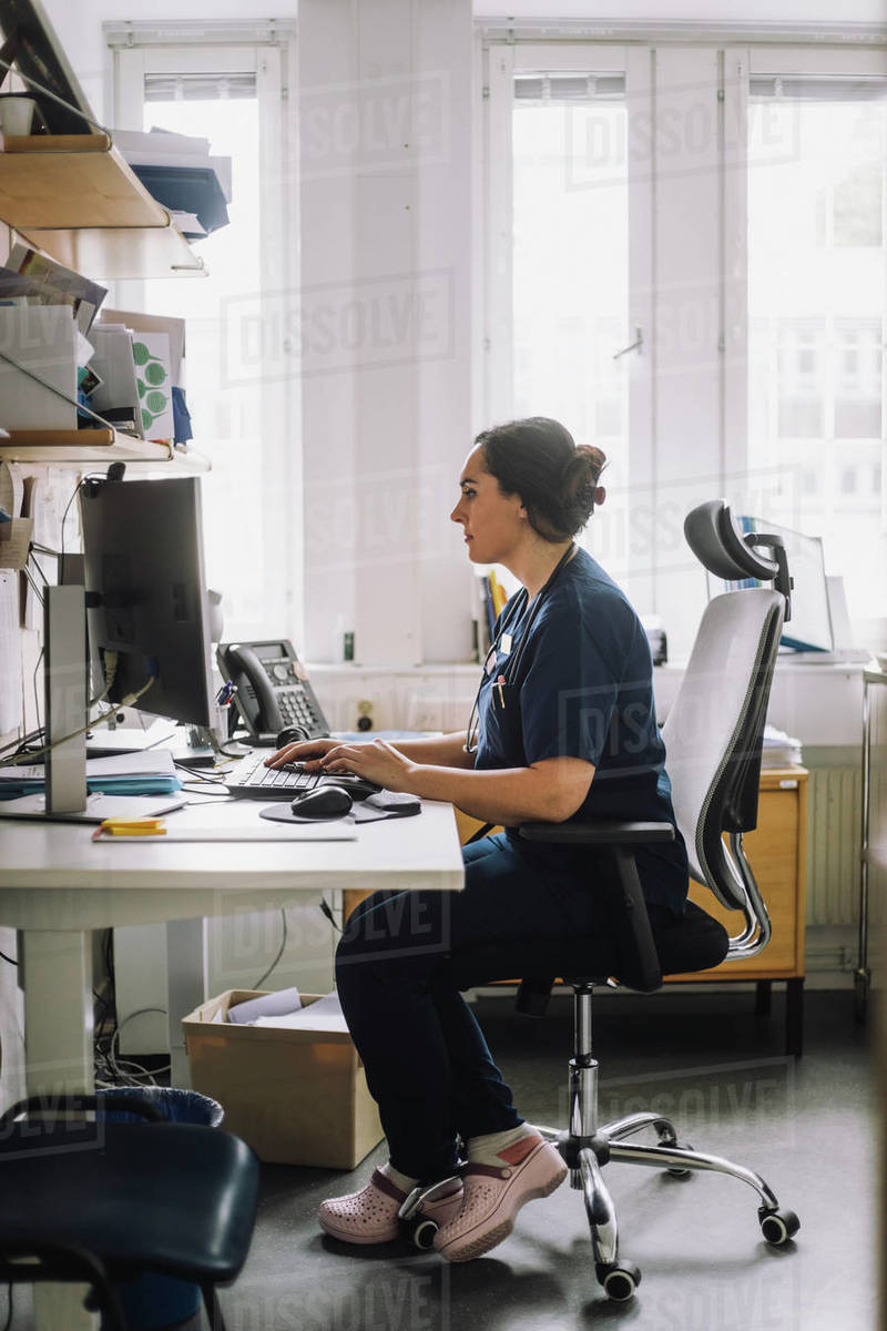 Side view of mature female nurse working on computer while sitting at ...