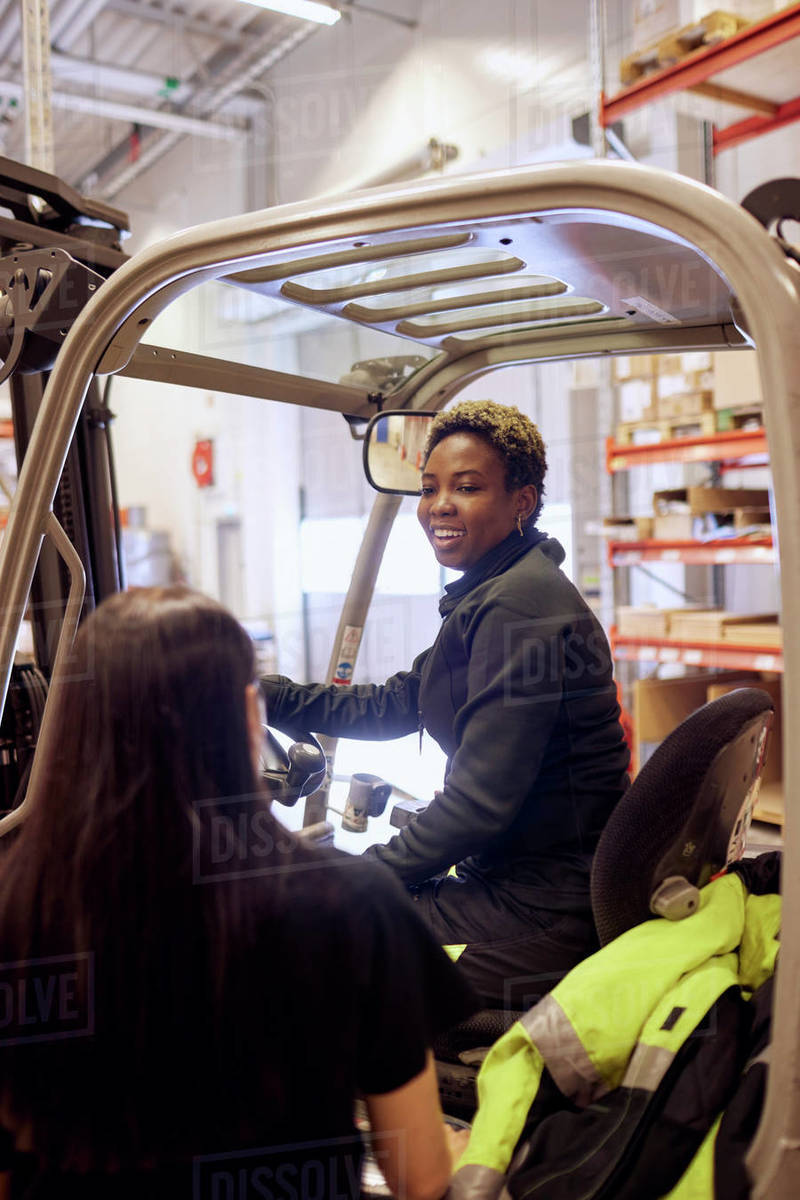 Smiling female forklift operator talking with coworker in distribution ...