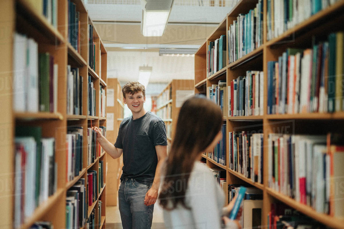 Happy students searching books on bookshelf in library at university ...