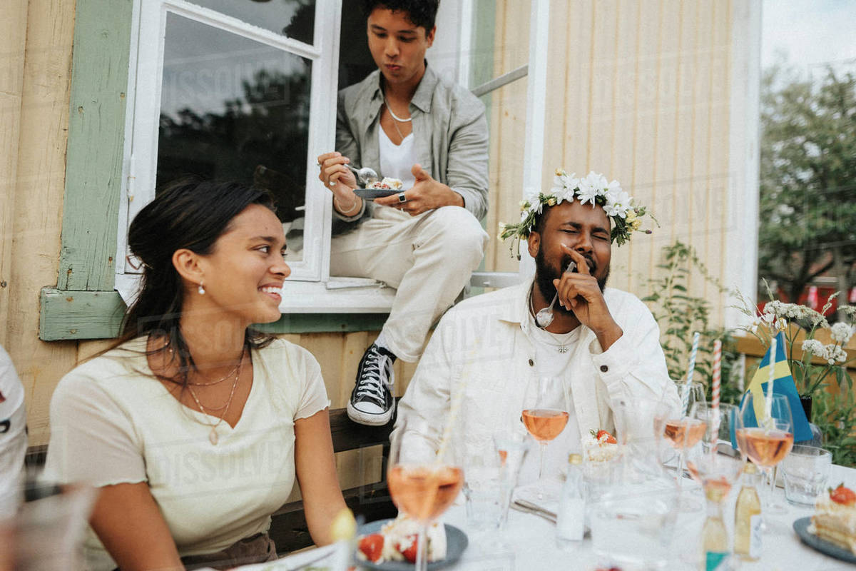 Young man laughing while eating cake with friends during dinner party ...