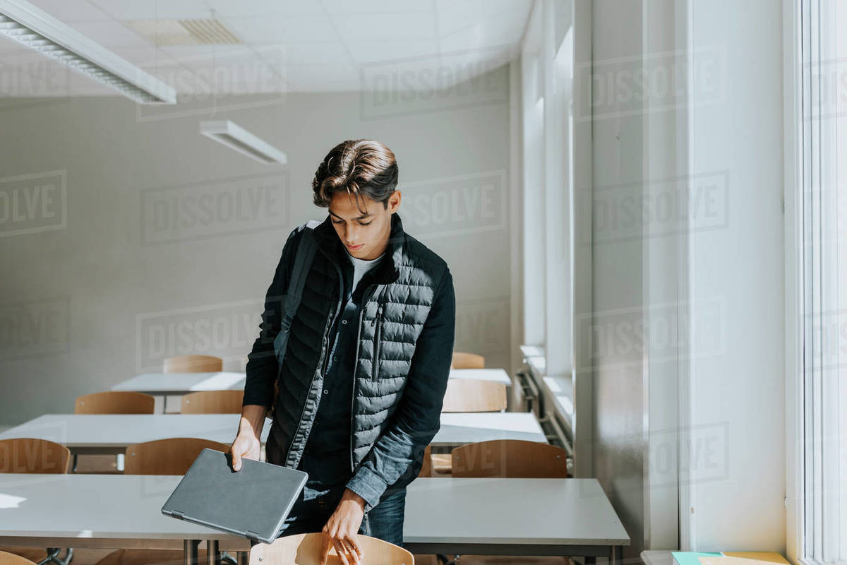 Teenage boy holding laptop while standing in classroom - Royalty-free ...