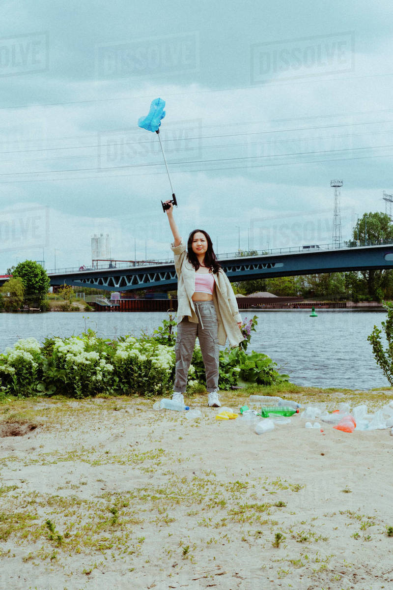 Full length portrait of confident young woman picking garbage near ...